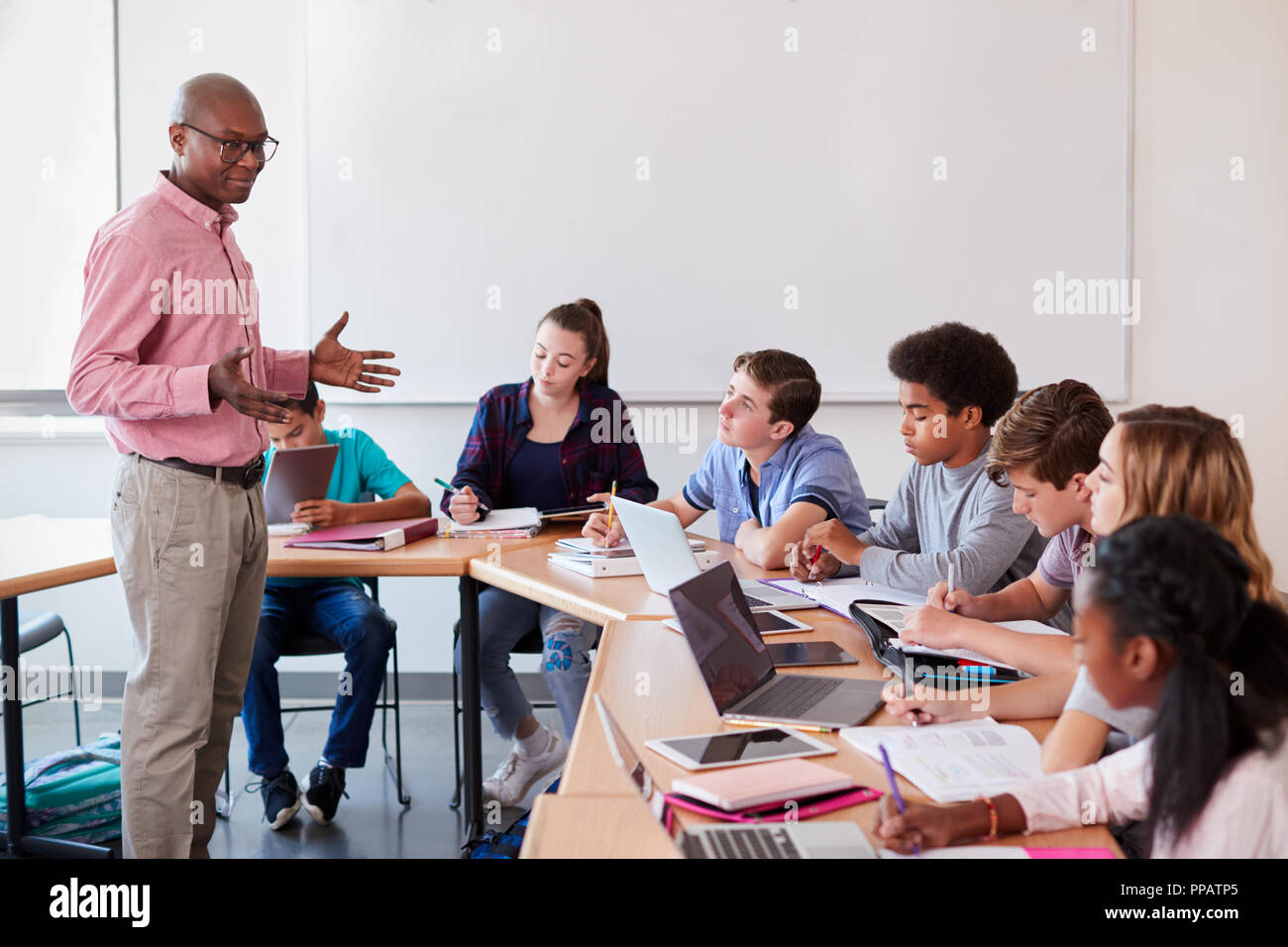 High School Teacher Talking To Pupils Using Digital Devices In ...