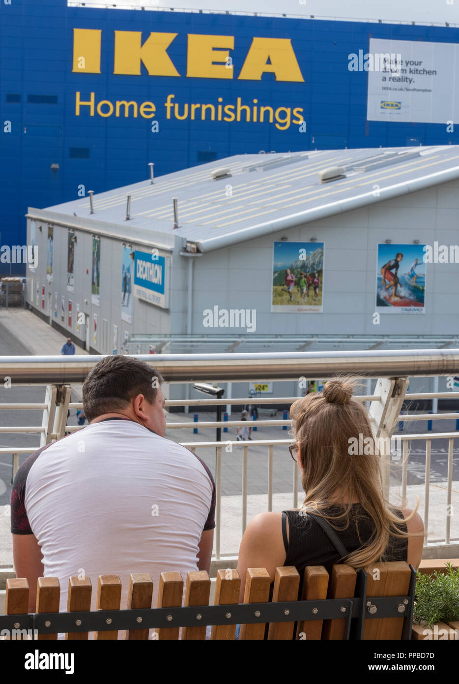 young couple sitting outside of west quay shopping centre in southampton with IKEA in the ...