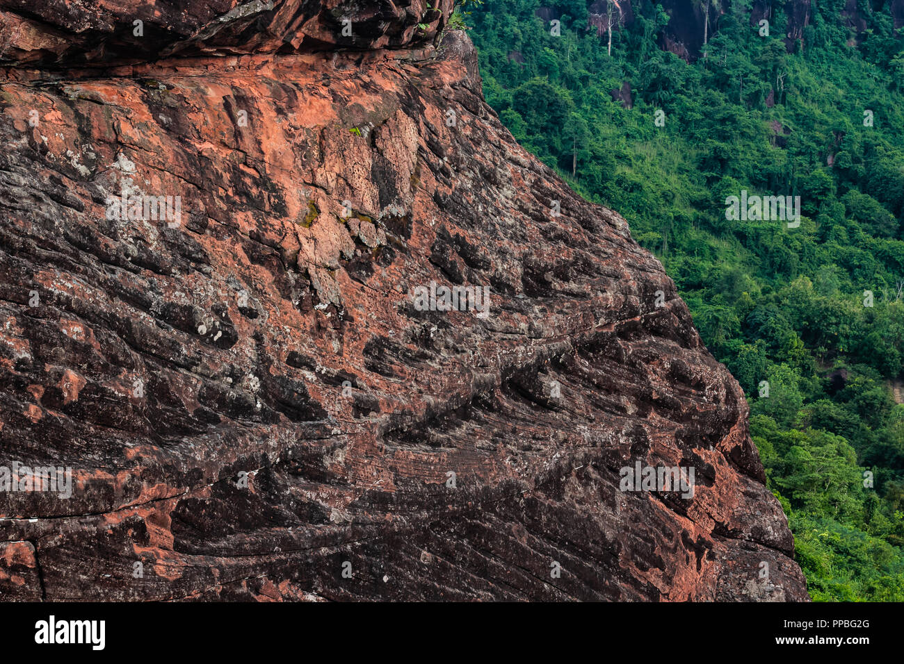 Looking off a mountains edge at a textured red/brown rock face high ...