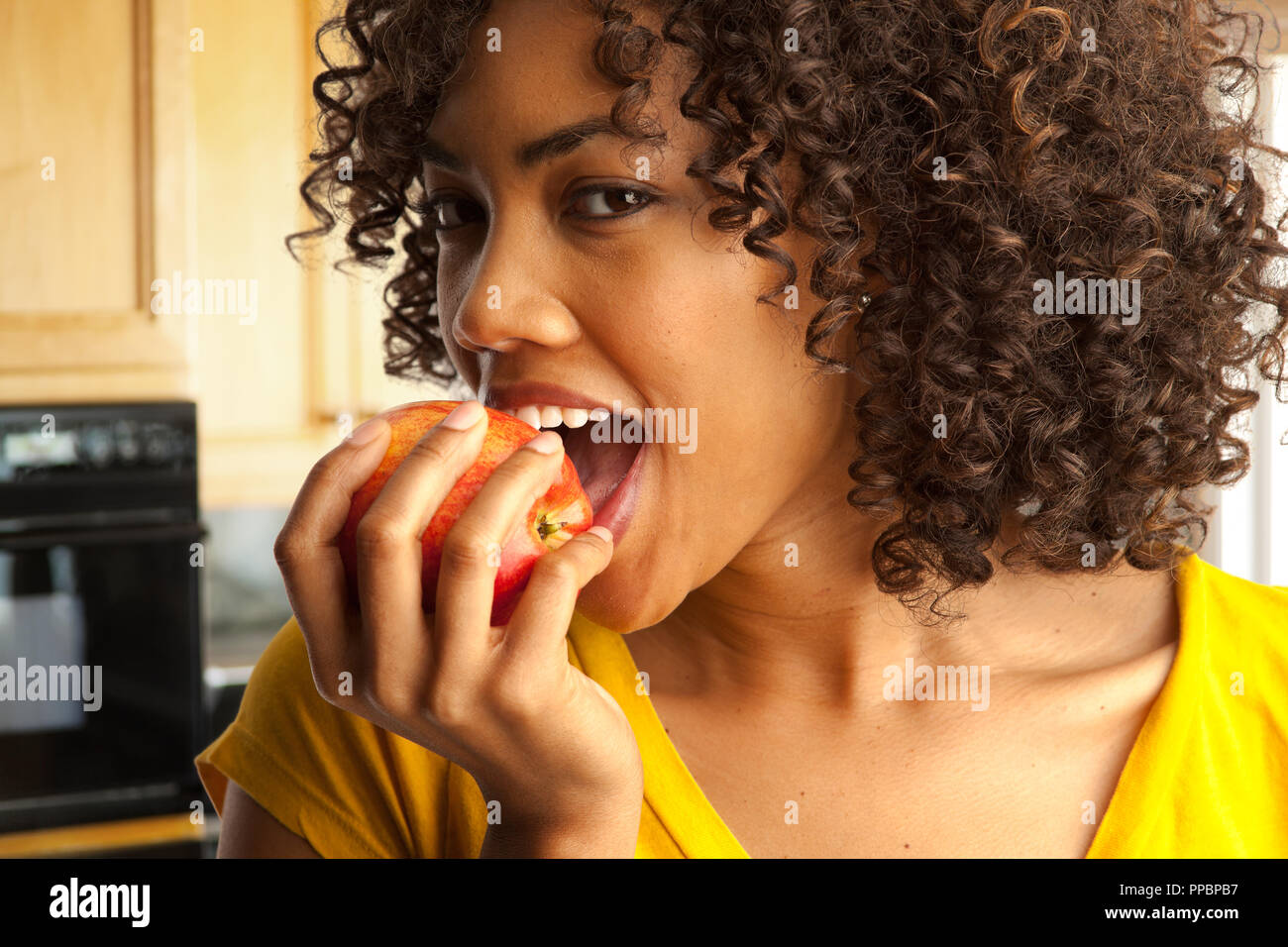 Portrait of millennial black woman taking bite of apple inside home ...