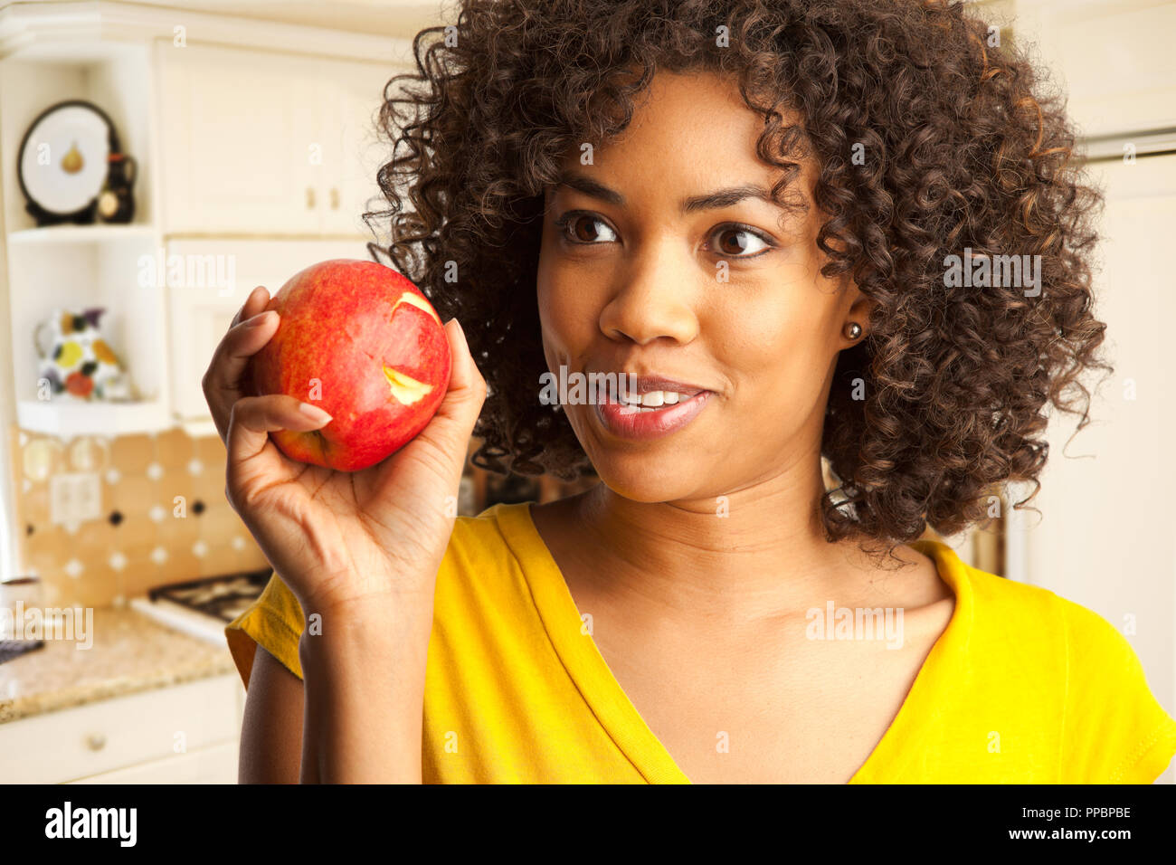 Portrait of millennial black woman taking bite of apple inside home ...