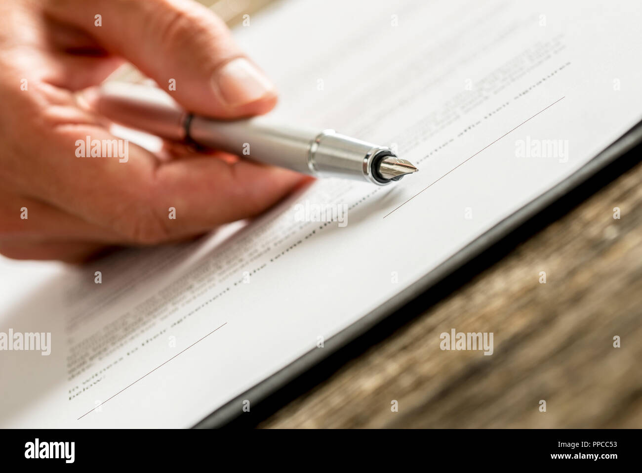 Closeup of male hand holding an ink pen pointing with its end on a line ...