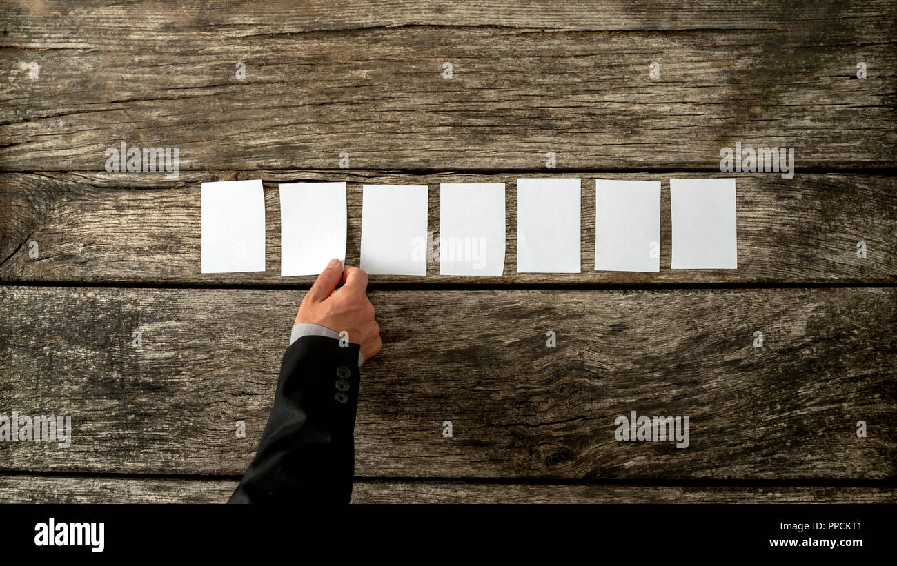 Overhead view of male hand in business suit placing seven blank white ...
