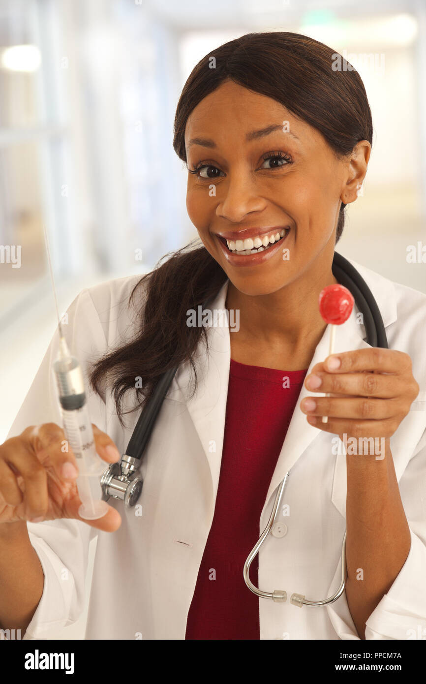 Portrait of happy young female doctor holding candy and syringe ...