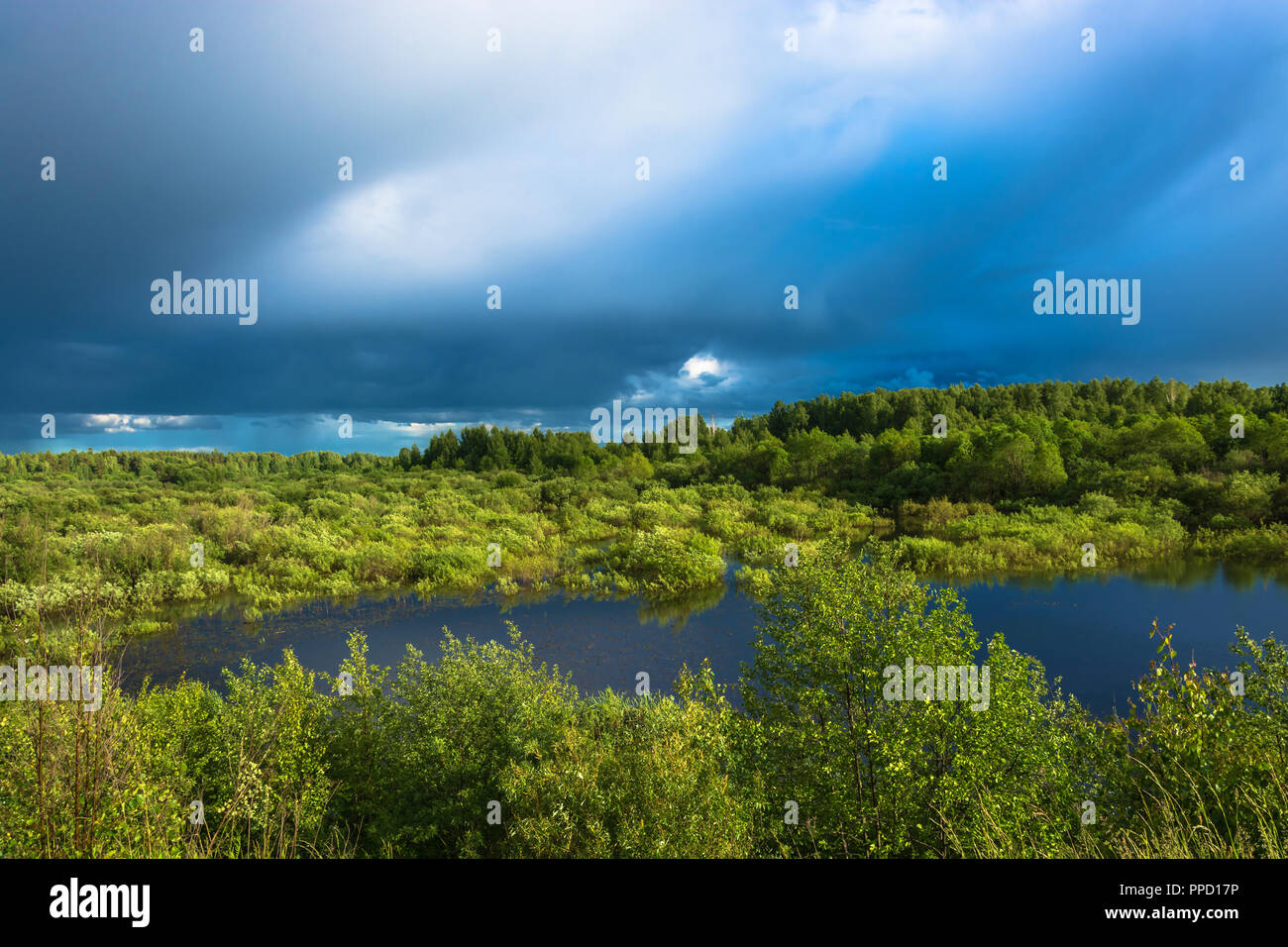 Beautiful landscape with a small lake, sunlit and disturbing storm sky ...