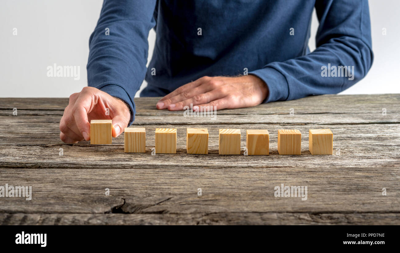 Front view of a man placing eight blank wooden cubes in a row on ...