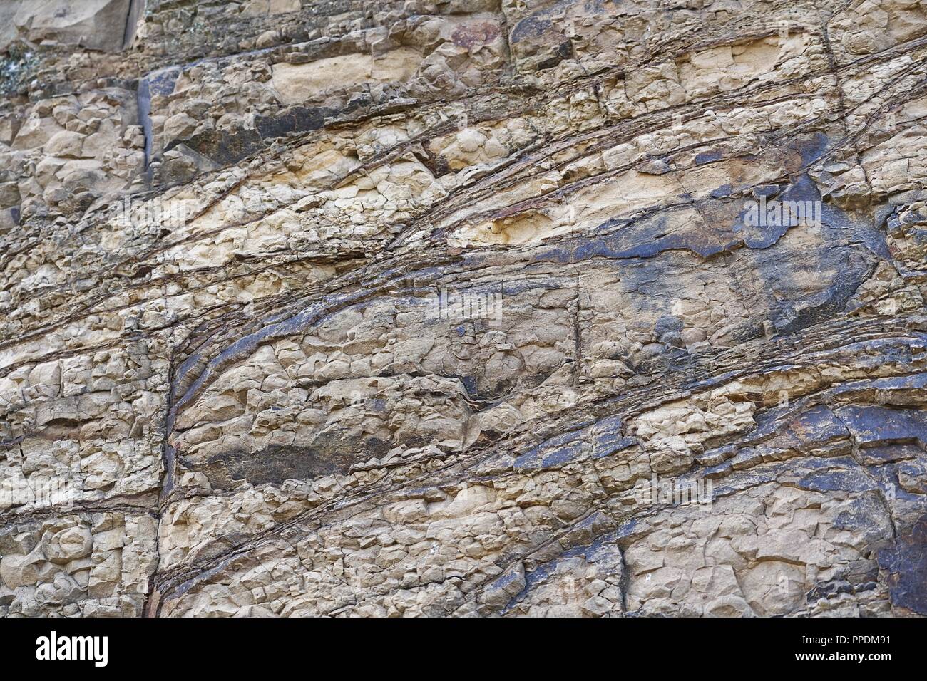 Weather eroded cliff face near a beach showing severe cracking and ...