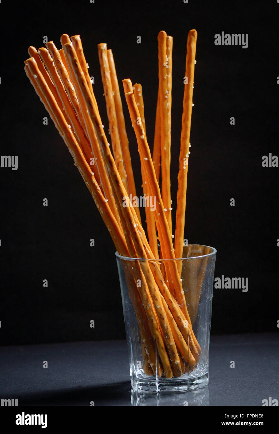 Pretzel sticks in small glass on black background Stock Photo - Alamy