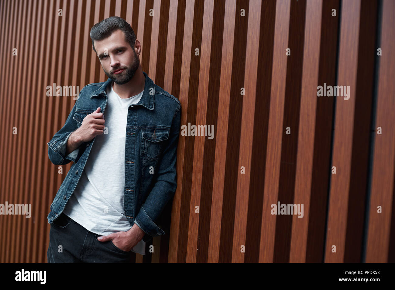 Freestyle. Young man standing leaning on wooden wall isolated looking ...