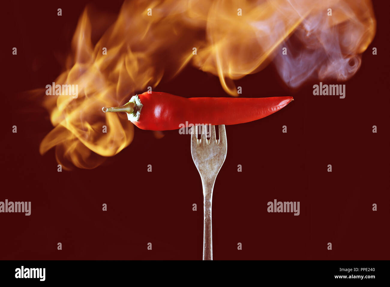 chili pepper red on fire on a dark red background Stock Photo - Alamy