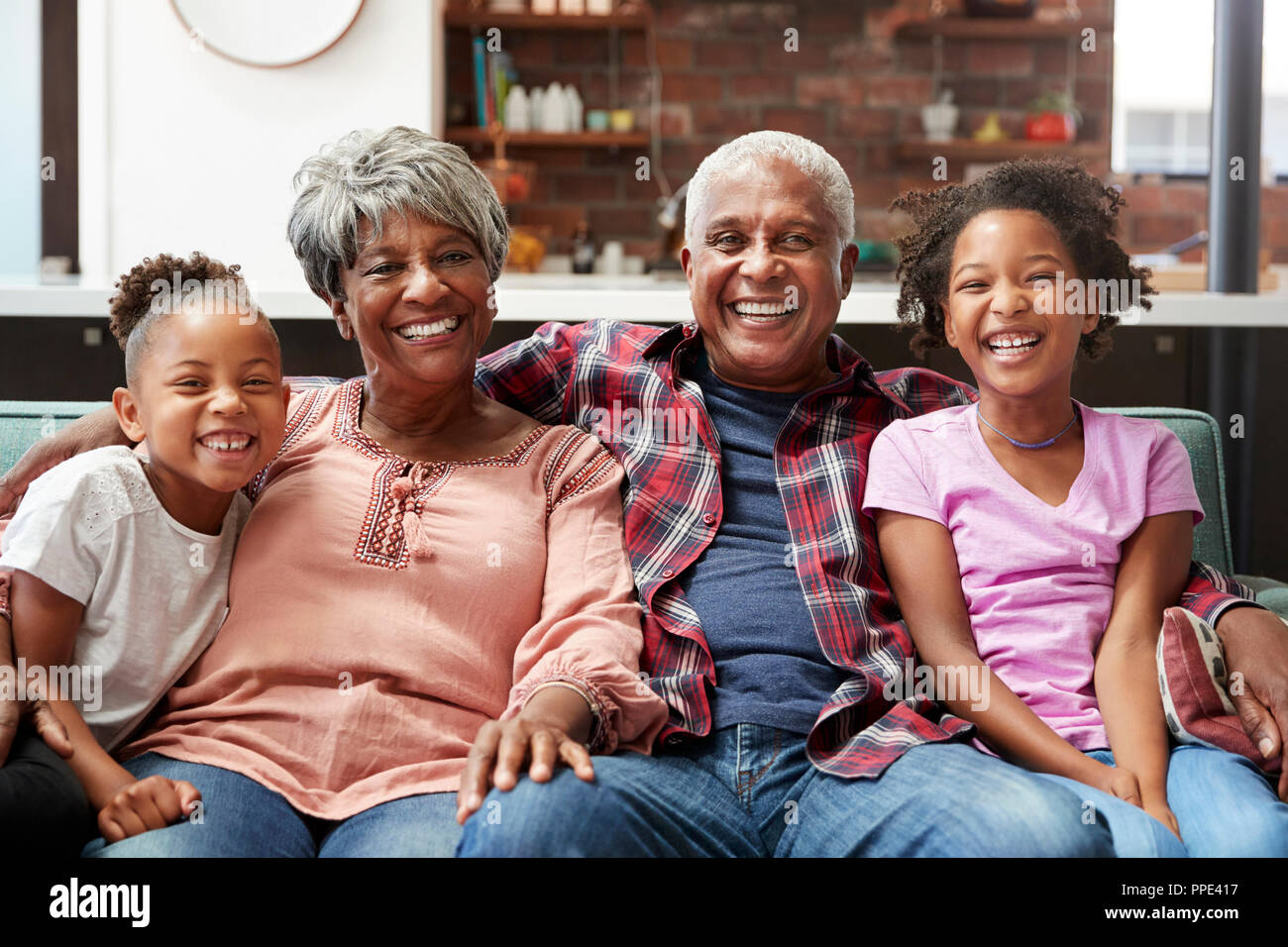 Portrait Of Grandparents Sitting On Sofa At Home With Granddaughters ...