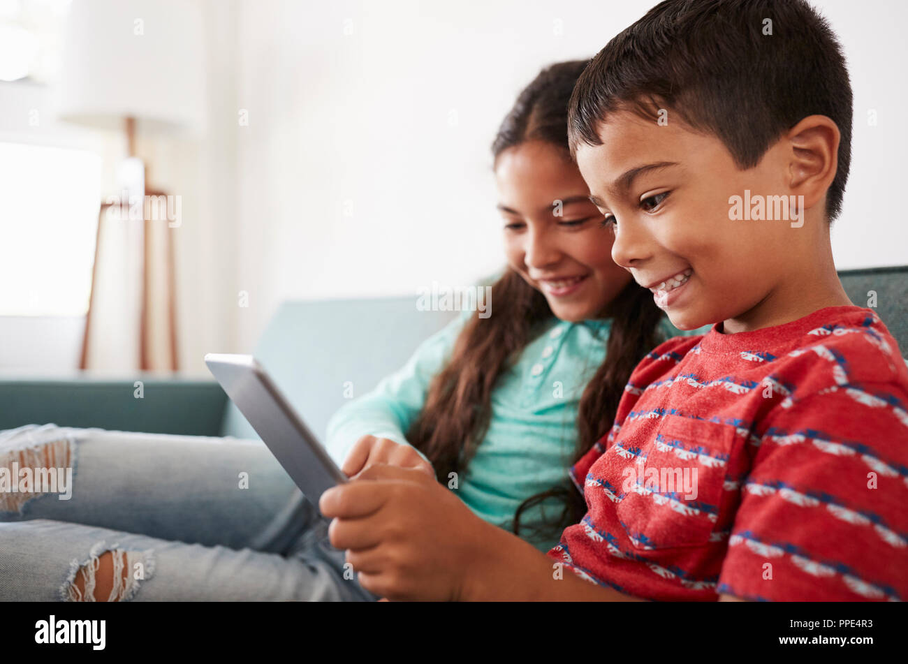 Brother And Sister Sitting On Sofa At Home Having Fun Playing On Digital Tablet Together Stock
