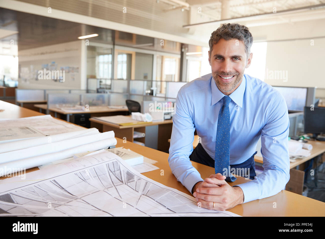 Male architect leaning on desk with plans looking to camera Stock Photo ...