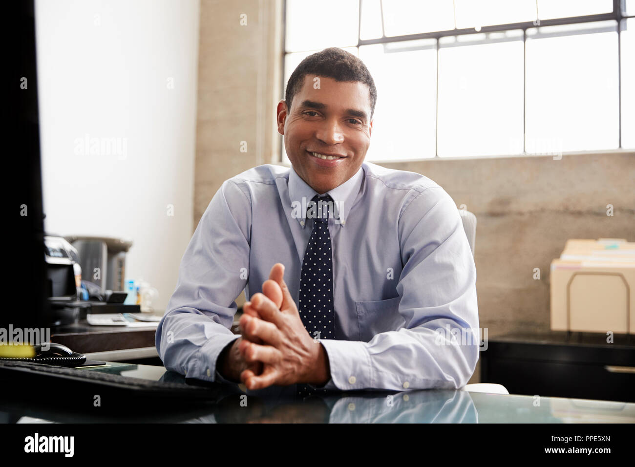 Mixed race businessman at an office desk smiling to camera Stock Photo ...