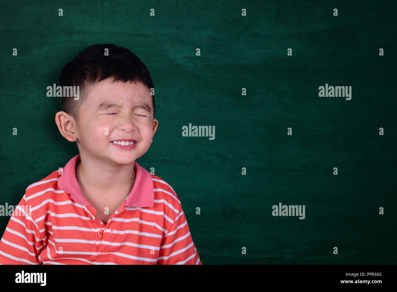 Happy Asian kid smiling on empty green chalkboard with copy space for ...