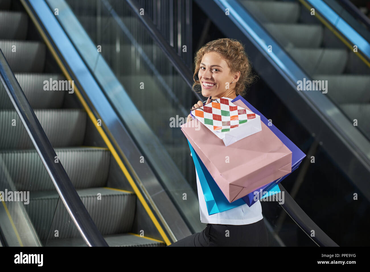 View from side of cheerful lady with shopping bags, looking at camera ...