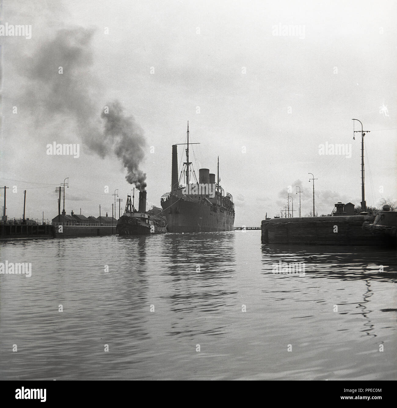 London docks 1950s, a steam driven tugboat pulls a large steamship in ...