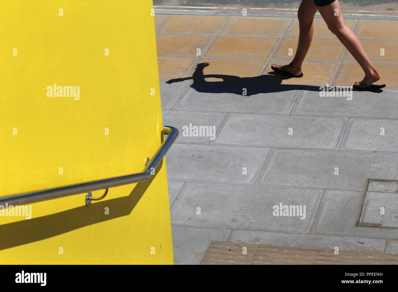 shadow of pedestrian stretching arms on pavement, next to yellow wall ...