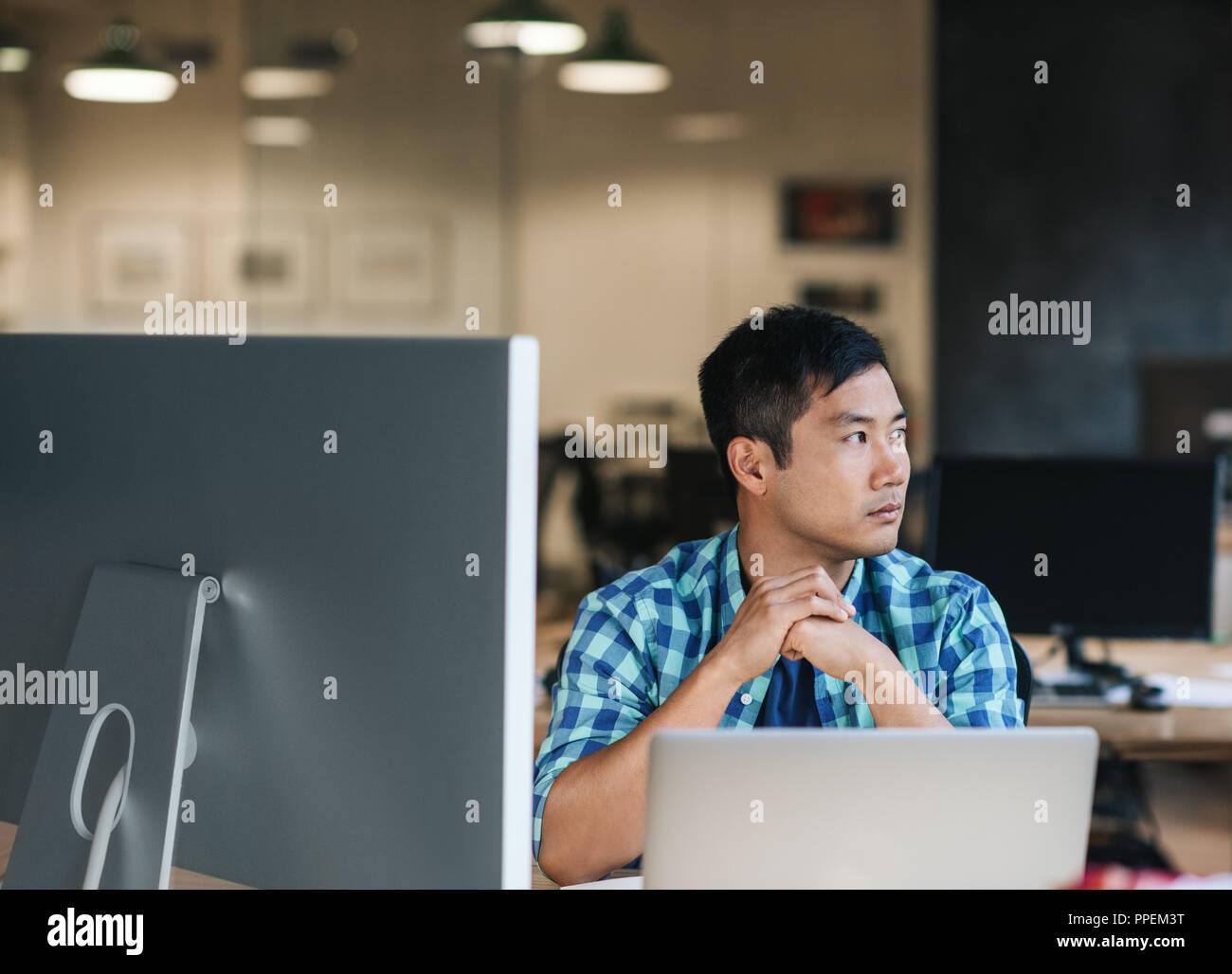 Young Asian designer sitting at his desk thinking about work Stock ...