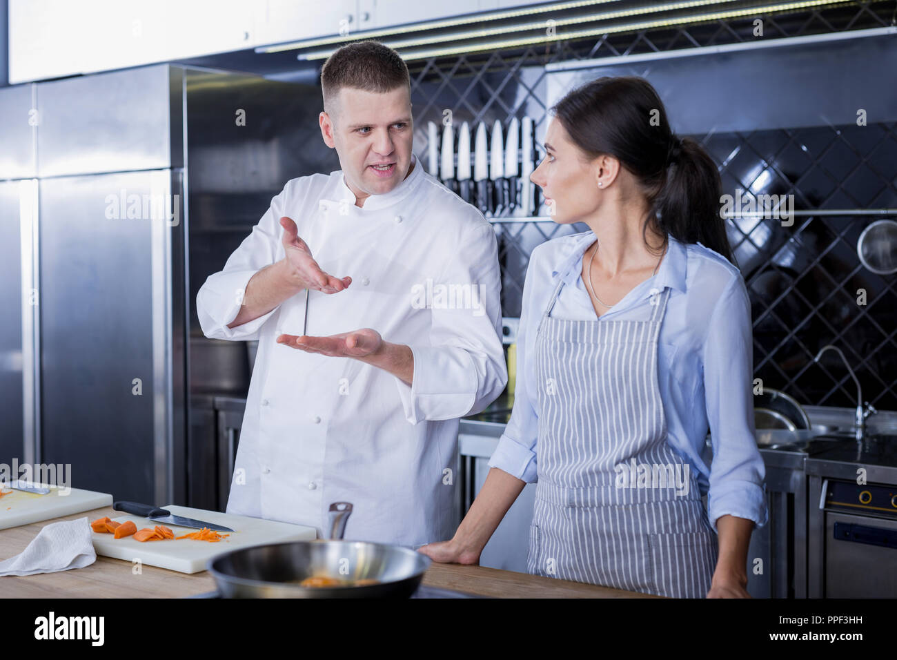 Serious cook giving different pieces of advice to a young cook Stock ...