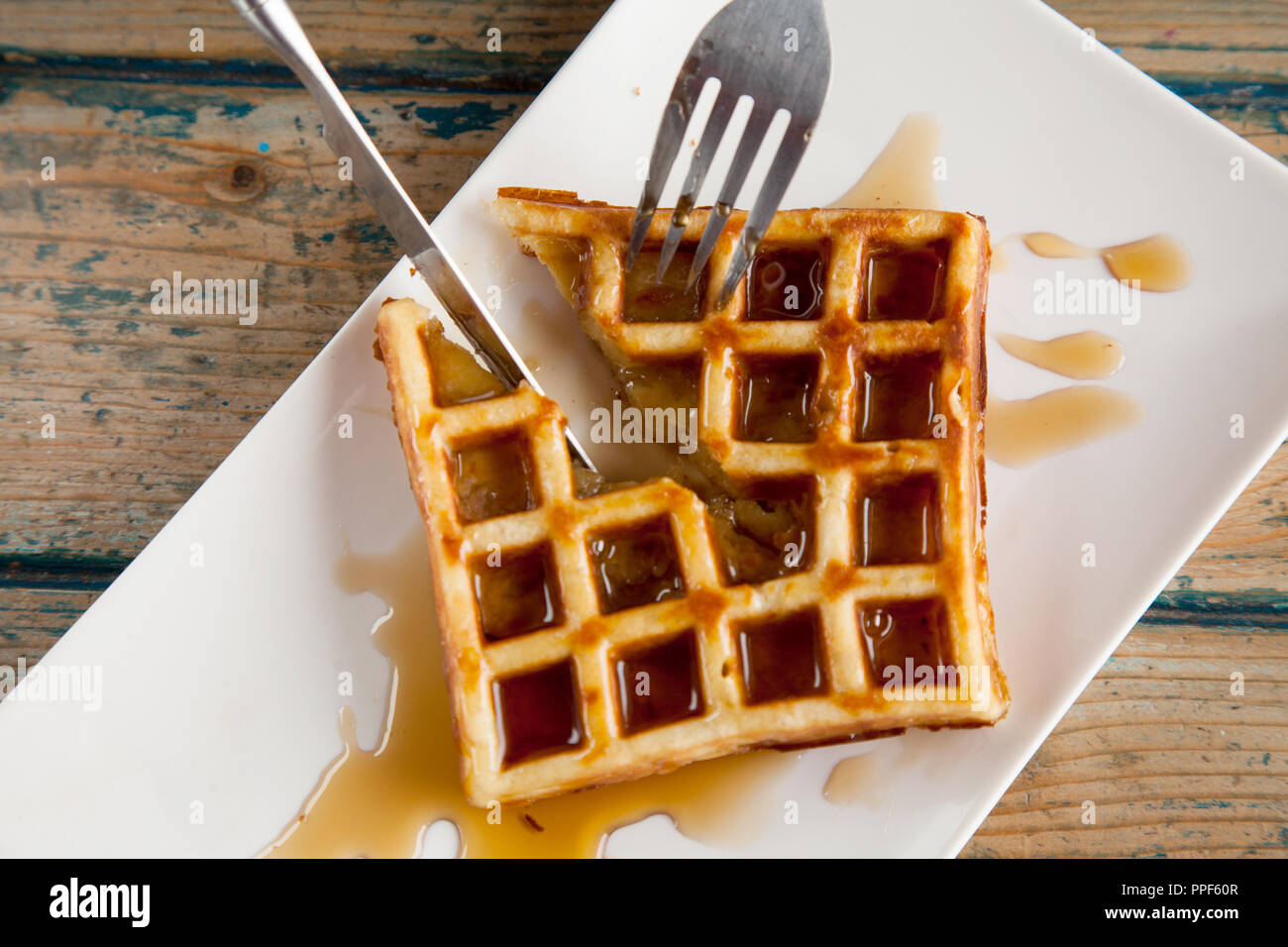 Waffle with maple syrup cutting in half with knife and a fork Stock ...