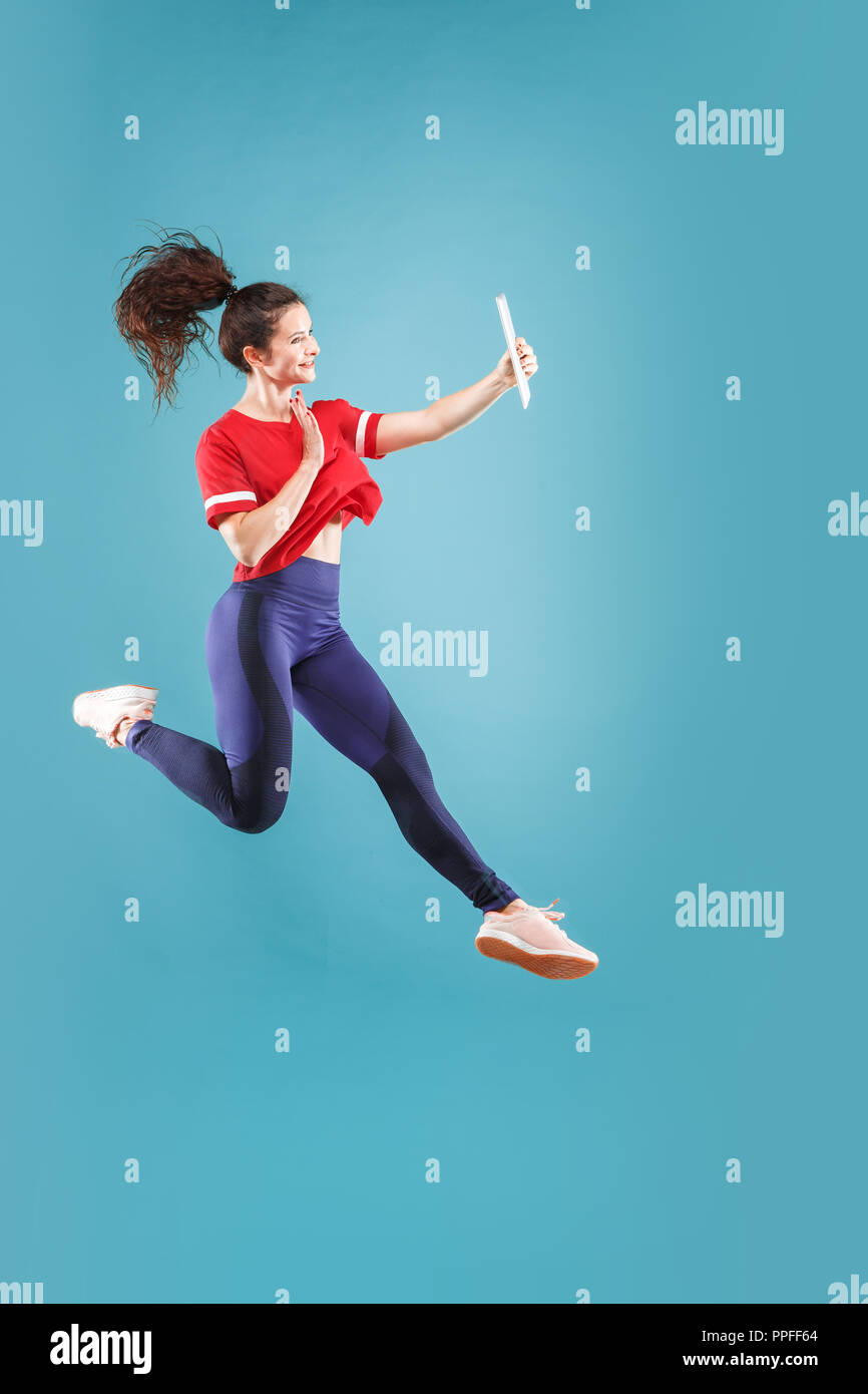 Gadget in modern life. Jump of young woman over pink studio background ...