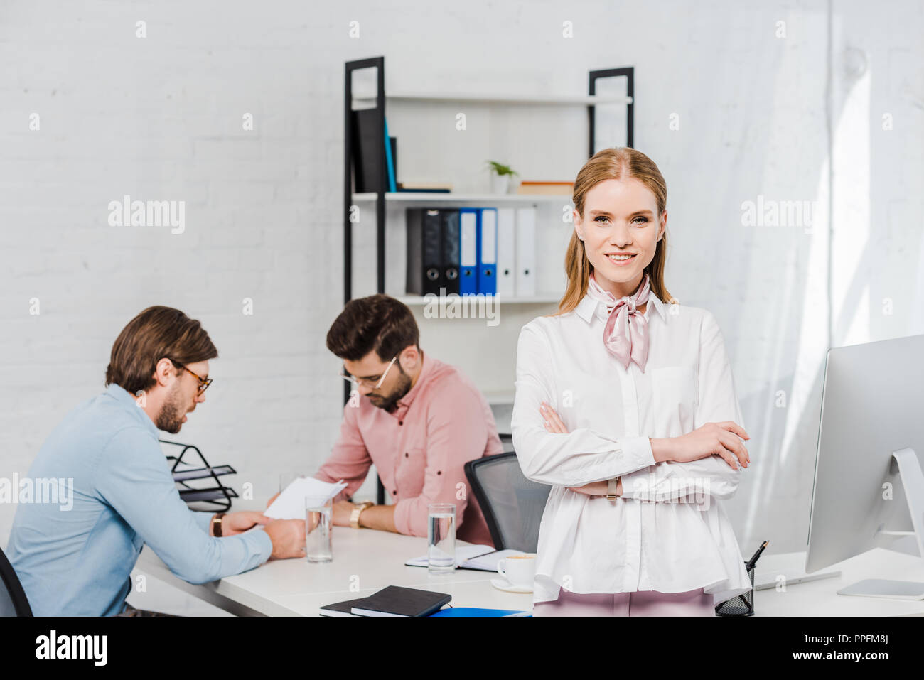 smiling young businesswoman with crossed arms looking at camera and ...