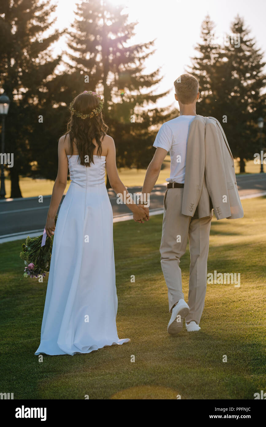 back view of wedding couple holding hands and walking outdoors Stock ...