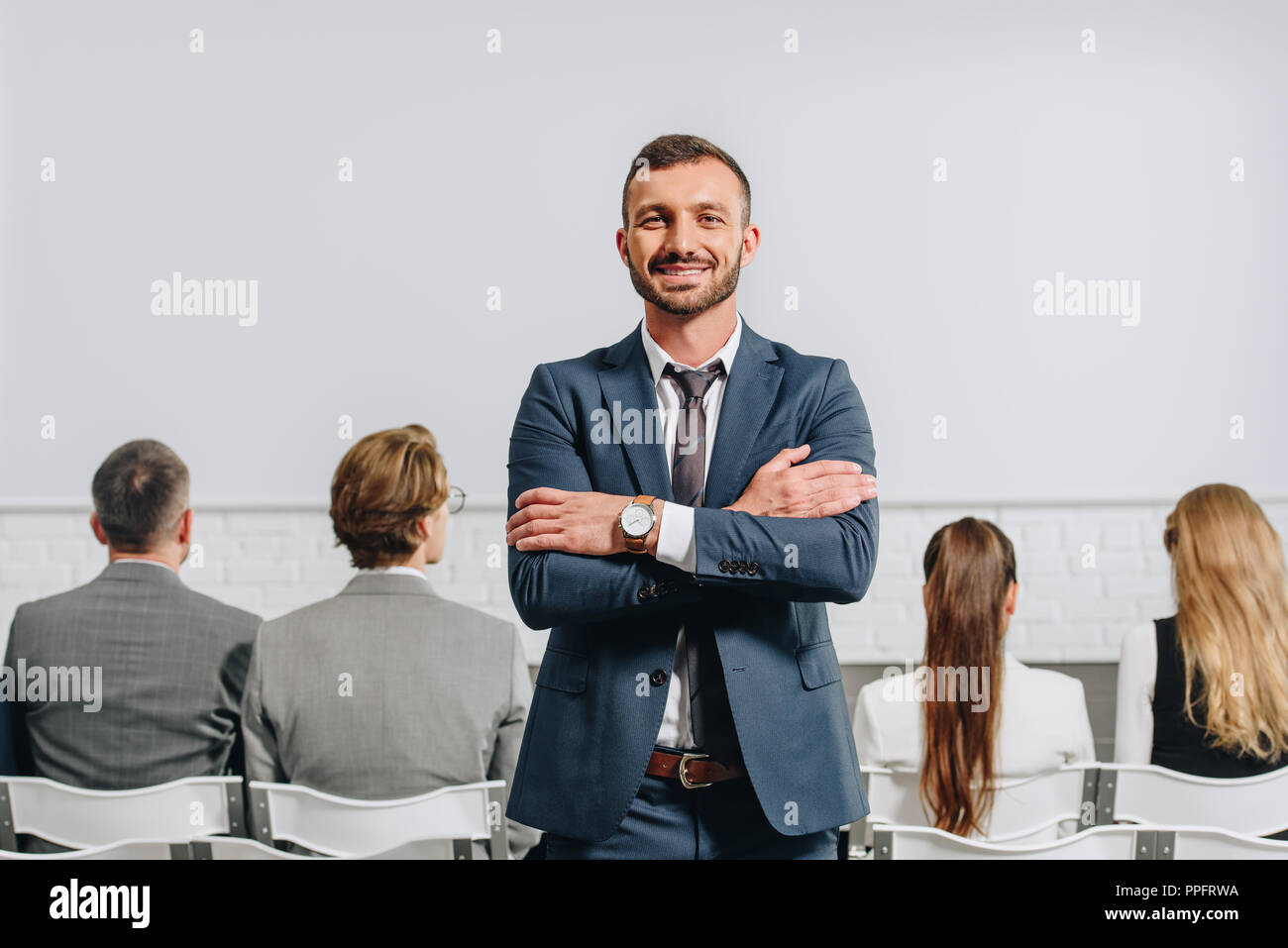 smiling coach with crossed arms looking at camera during business ...
