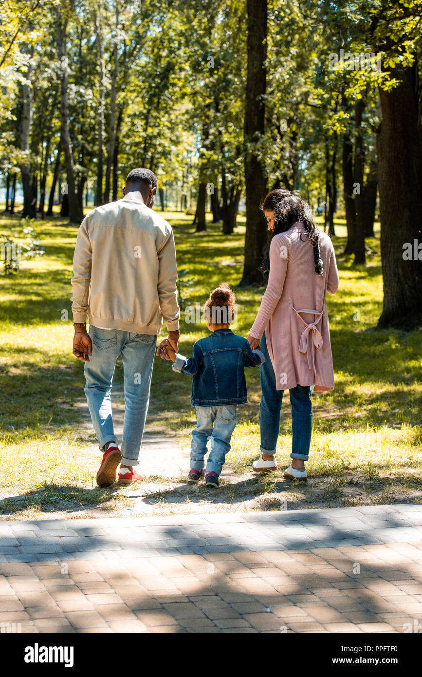 back view of african american parents and daughter walking in park on ...