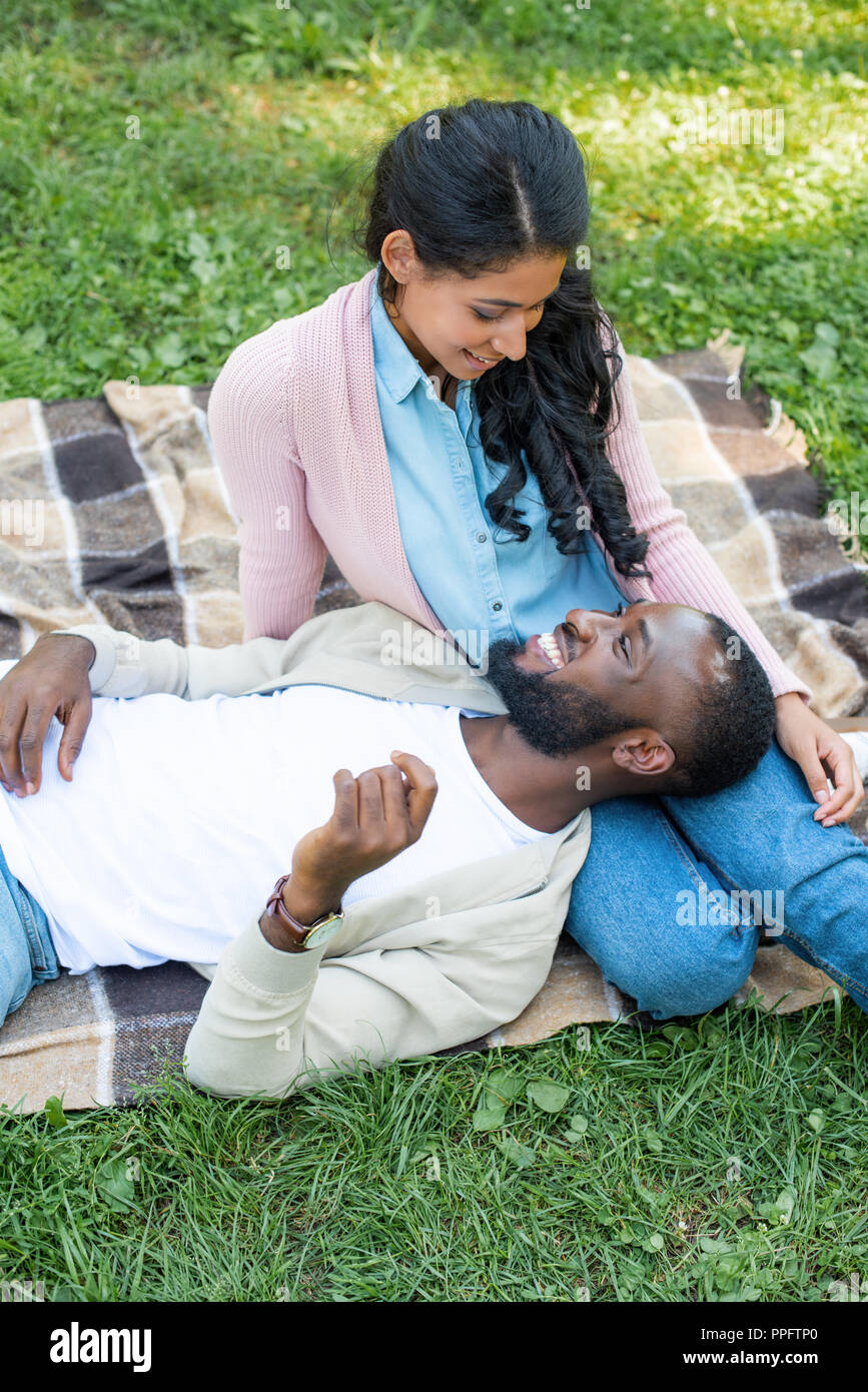 high angle view of happy african american boyfriend lying on girlfriend ...