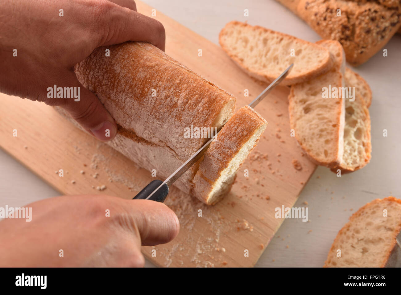 Chef slicing bread in slices on a cutting board in a kitchen bench. Top ...