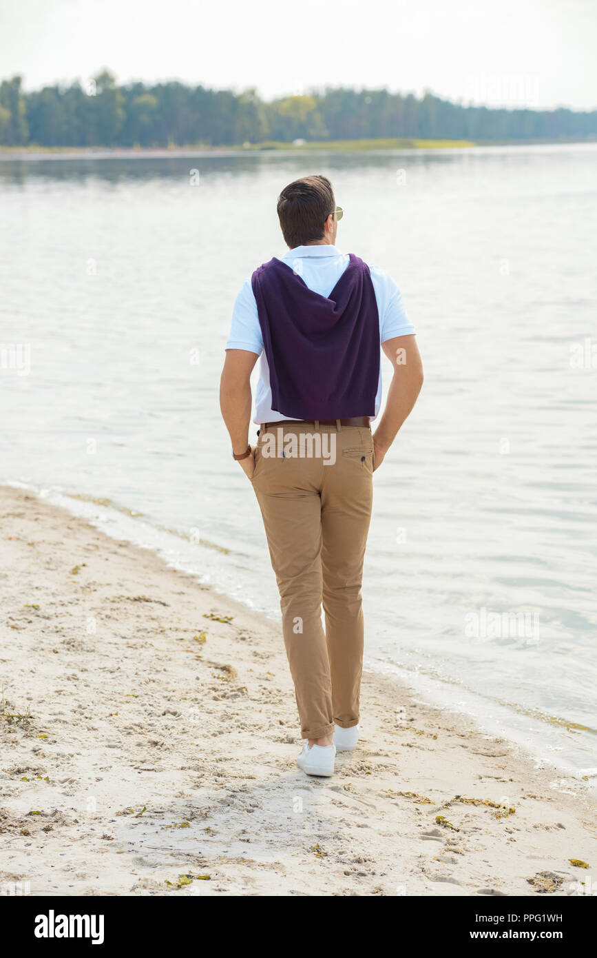 back view of stylish man walking alone on sandy riverbank Stock Photo ...