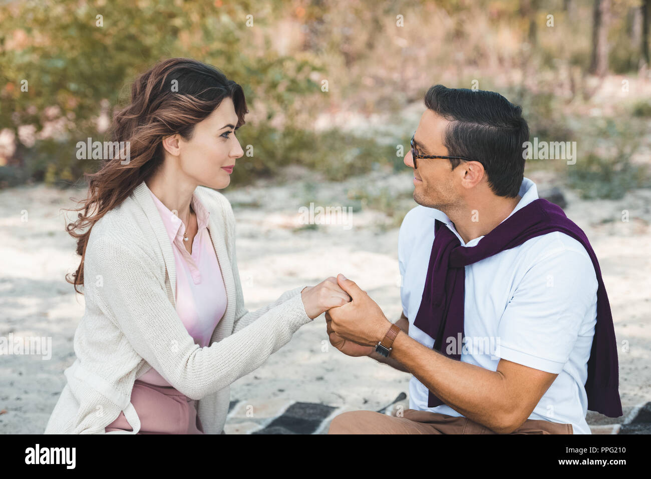 side view of romantic couple holding hands while resting on blanket on ...