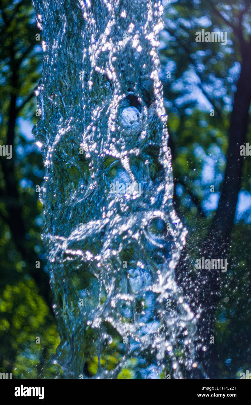 transparent falling water vertical flows against a blue sky and green ...