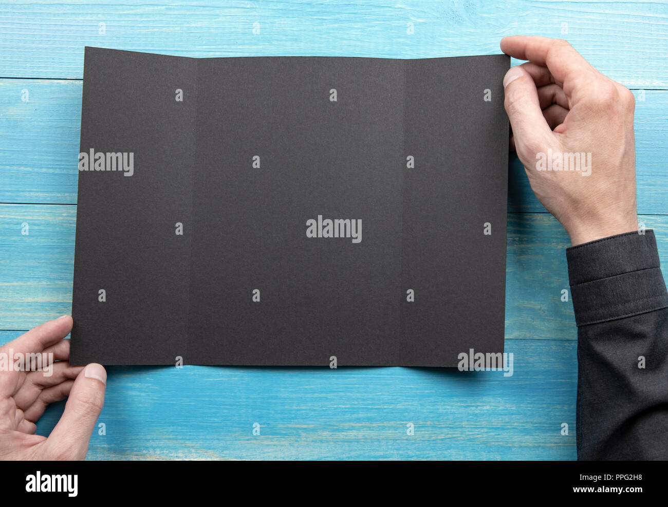 Mens hands holding empty black booklet on blue wooden background. View ...