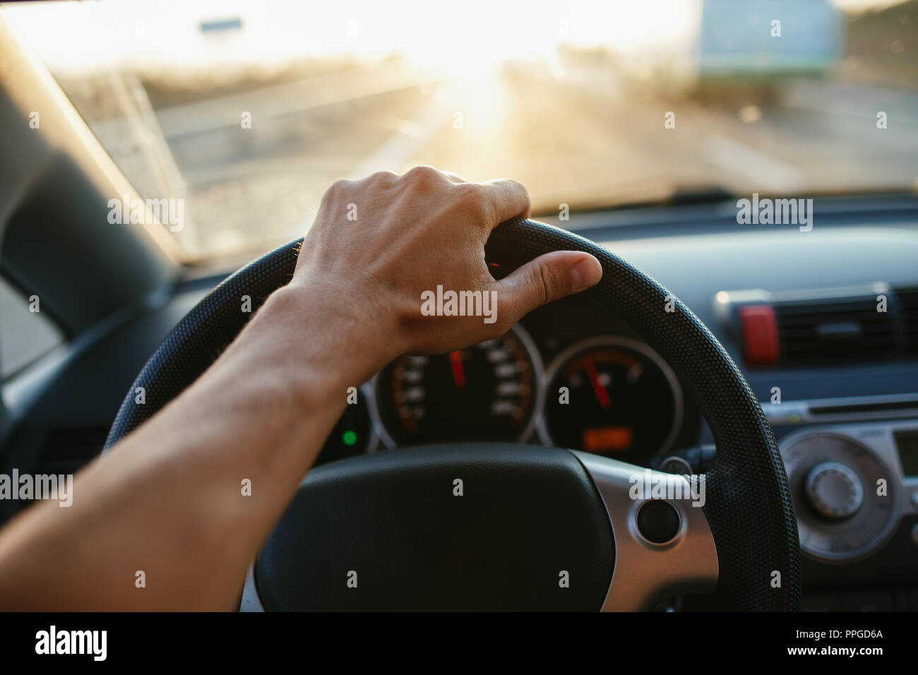 Selective focus man's hand on steering wheel, driving a car at sunset ...