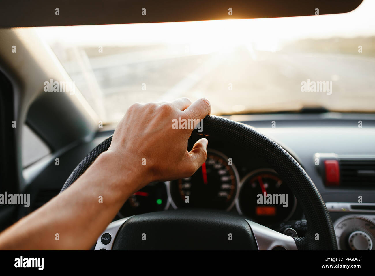Selective focus man's hand on steering wheel, driving a car at sunset ...