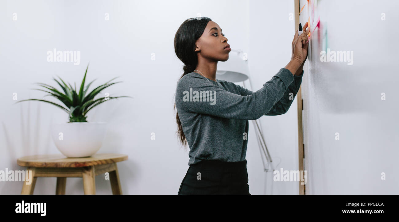 Young african woman putting post it note on white board in office ...