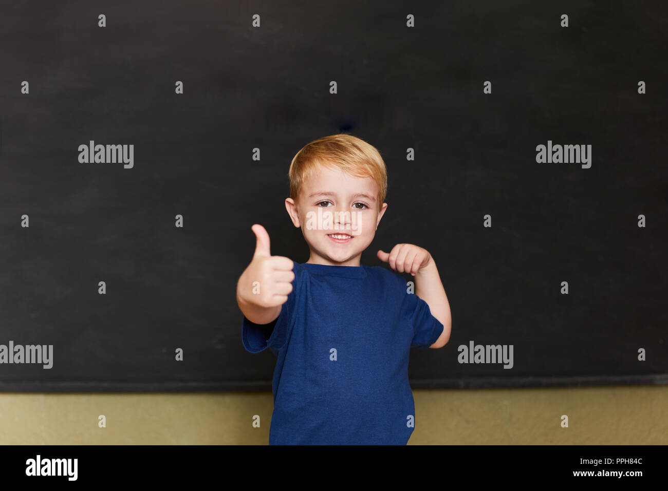 Student holds a thumbs up in front of blackboard in elementary school ...