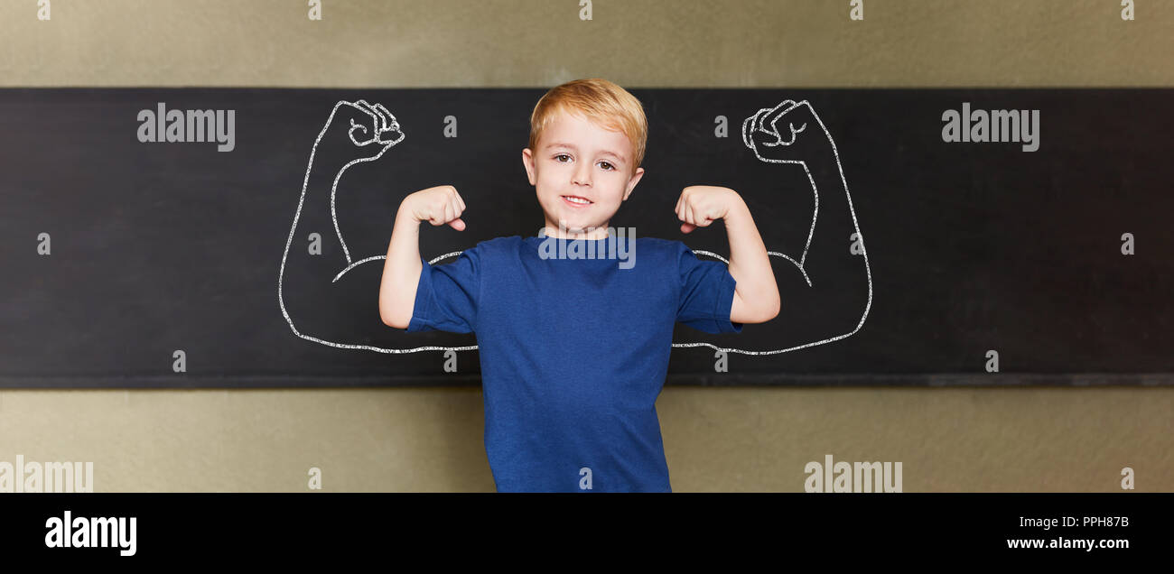 Confident child stands with muscles in front of the blackboard in a ...