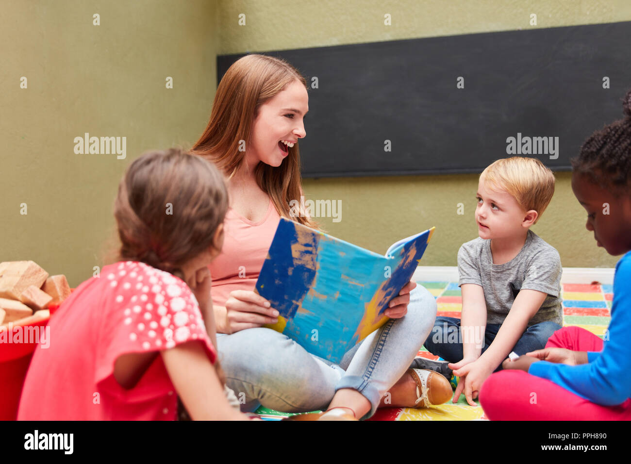 Happy teacher and children reading from a book in preschool or daycare ...