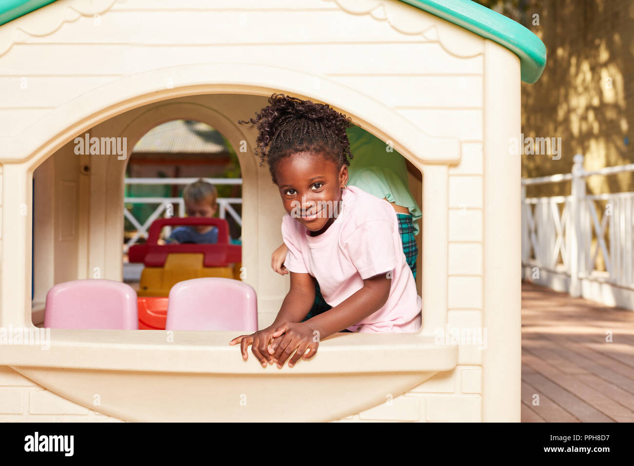African girl peers through window from play house in kindergarten or ...