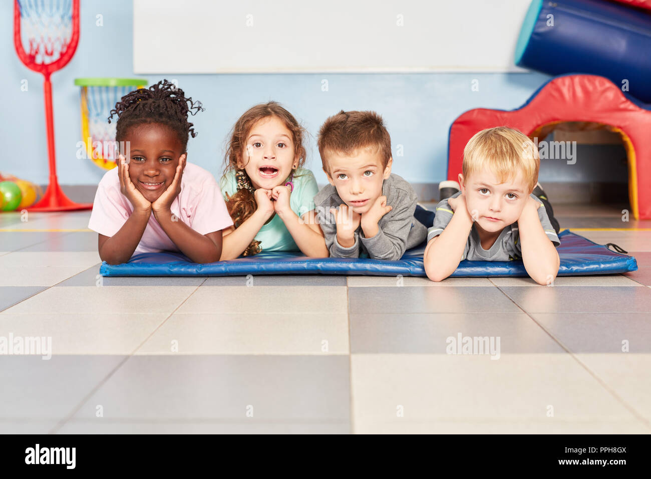 Four children lie on a mat in the gym of a multicultural elementary ...