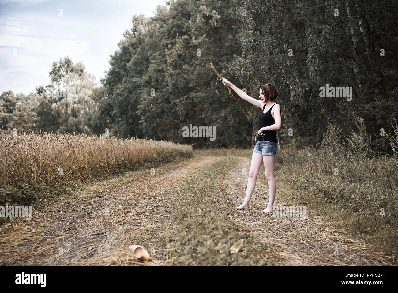 young girl walking barefoot on the ground road through field and forest ...
