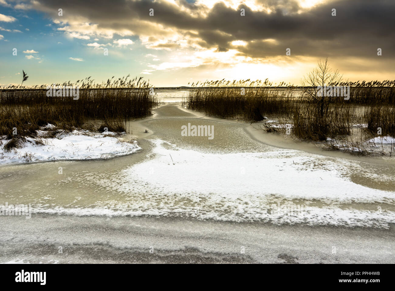 Winter landscape of lake with snow in moody scenery of sunset sky with ...