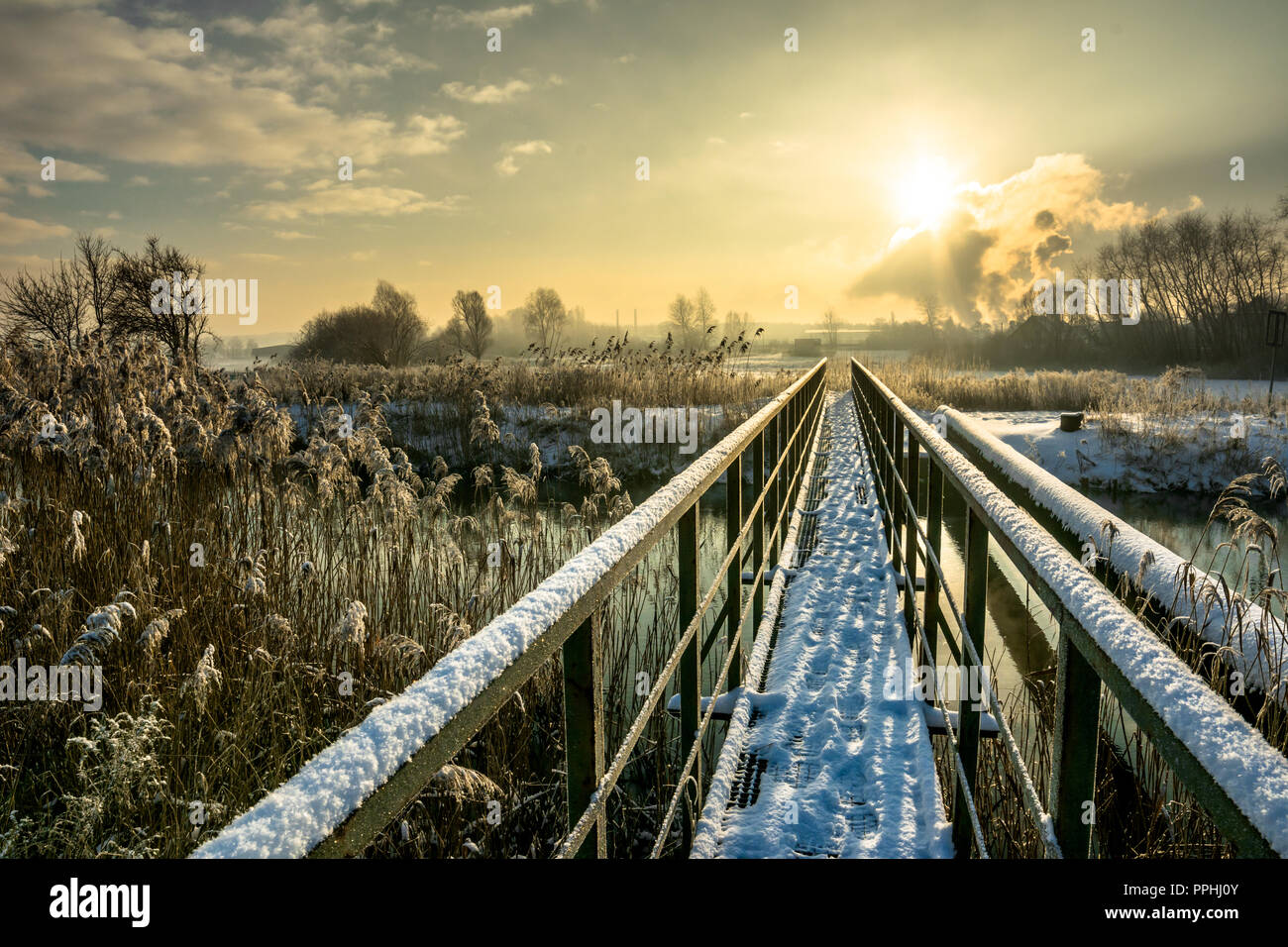 Winter landscape with footbridge across river, modern architecture in ...