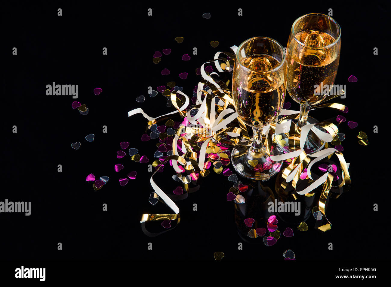 two glasses of champagne on a shiny black surface with confetti against ...