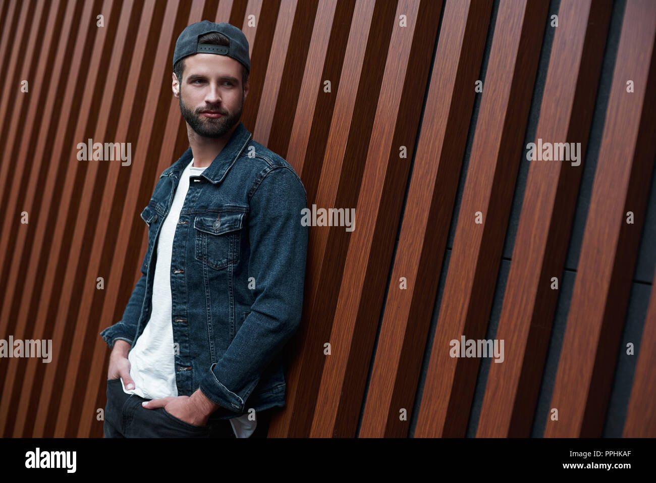 Freestyle. Young man standing leaning on wooden wall isolated looking ...