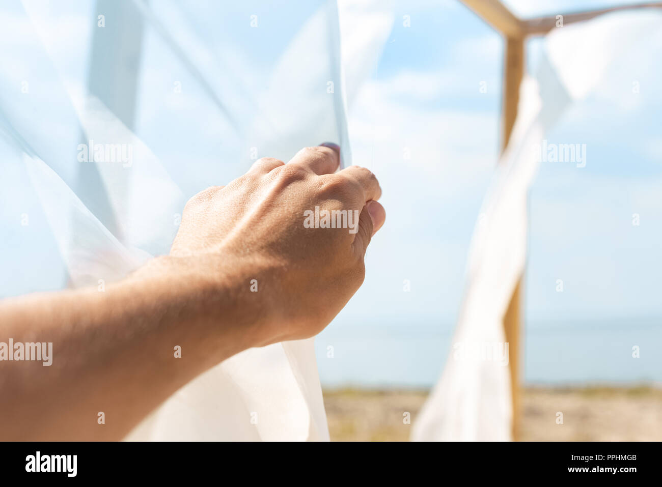 partial view of man holding white curtain lace with blue cloudy sky on ...